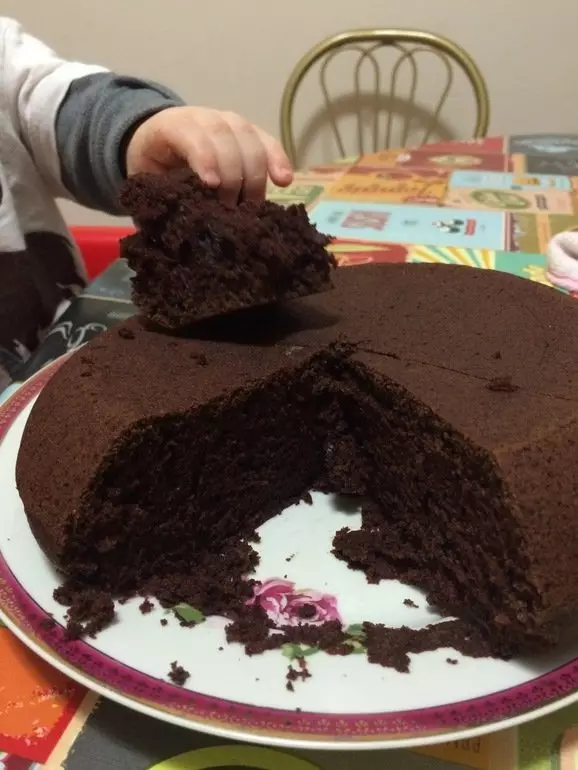 बच्चा चॉकलेट केक का एक टुकड़ा लेता है