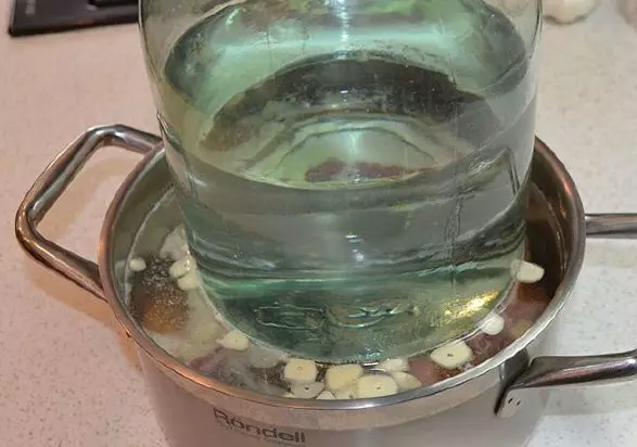 Salo v pánvi s vodou a česnekem pod zásuvkou sklenice s kapalinou
