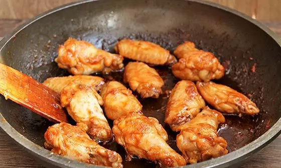 Спремна пилећа крила у сосу од соје од меденог соја у посуди са дрвеним сечивом