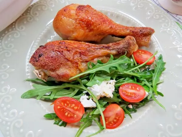Kaki ayam dengan kerak kemerahan di atas piring dengan salad arugula, ceri dan keju