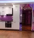 Połączenie fioletowego fartucha, białe meble i jasne tapety w kuchni