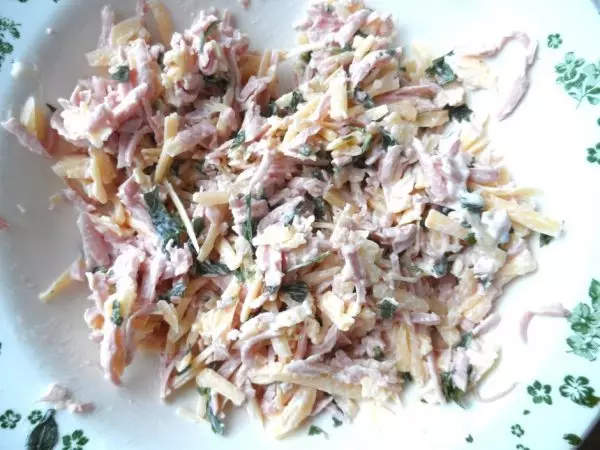 A mixture of boiled sausage, solid cheese, greenery and mayonnaise in a bowl
