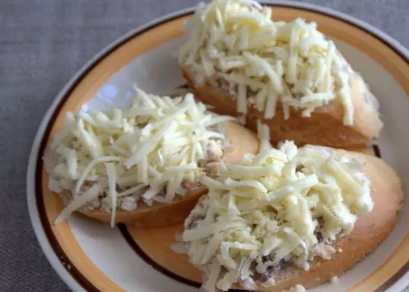 Slices of baguette with fish-egg mixture and grated cheese on a plate