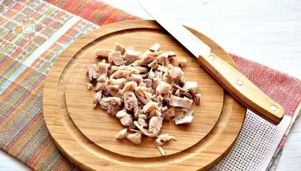 Sliced ​​with small pieces boiled chicken meat on a wooden cutting board with a knife