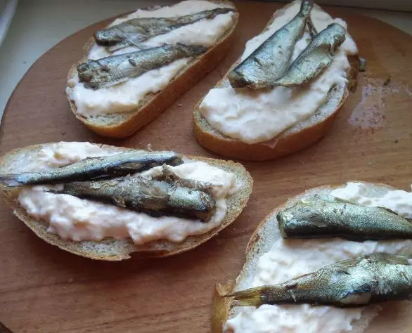 Billets for hot cheese sandwiches and sprats on a wooden cutting board