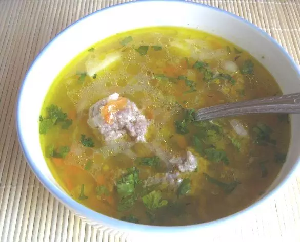 Supă cu chifteluțe și orez într-o placă de porțiuni cu o lingură de metal