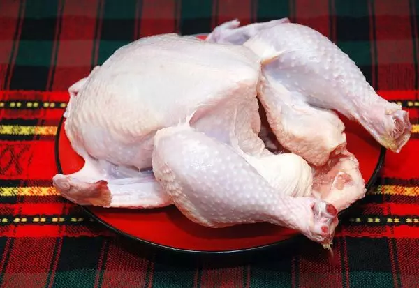 Carcassa de pollastre crua en una placa vermella a la taula