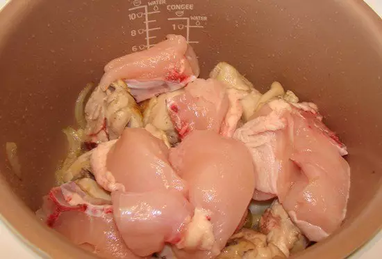 Segmenten van rauwe kip in een kom Multicooken met een gebakken ui