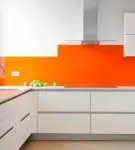 Kombinasi perabot putih lan apron oranye ing desain pawon