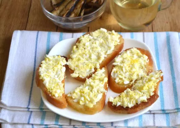 Potongan roti putih panggang dengan mayones dan telur gigih di atas piring