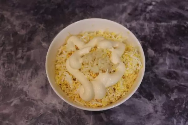 Krullende gekookte eieren, stevige kaas, gehakte knoflook en mayonaise in een witte kom op de tafel