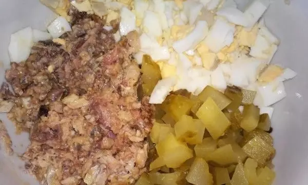 Skivad saltade gurkor och ägg i en skål med hackad konserverad fisk