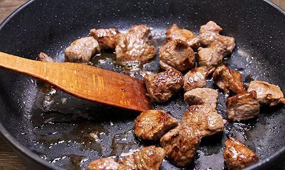 Potongan daging panggang dalam kuali dengan spatula kayu