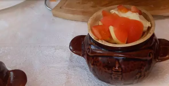 Oală ceramică cu bucăți de roșii și un pat pe masă