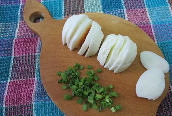 Nakrájené s plátky vařená vejce a nasekané zelené cibule na dřevěné prkénko
