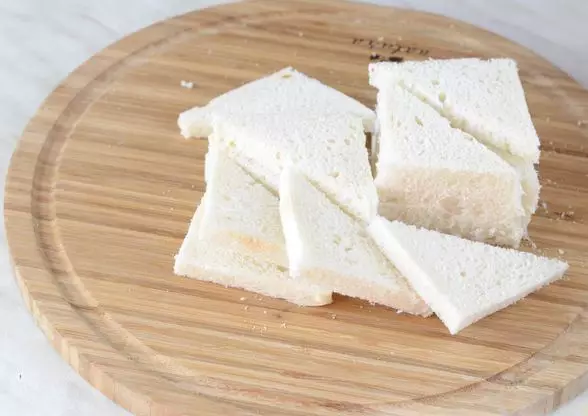 ขนมปังขาวชิ้นไม่มีเปลือกโลกบนกระดานตัดรอบ