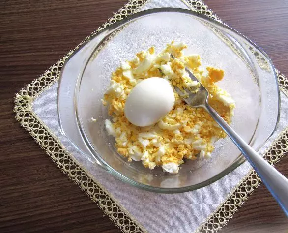 Grilled boiled eggs and a whole boiled egg in a glass container with a metal fork
