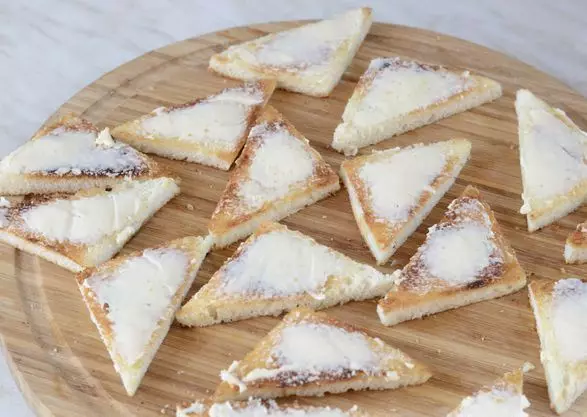 Triangular croutons made of white bread with melted cheese on a round cutting board
