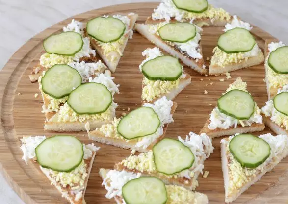 Trikotne sendviče s kuhanim jajcem in sveže kumare na rezalni plošči iz lesa