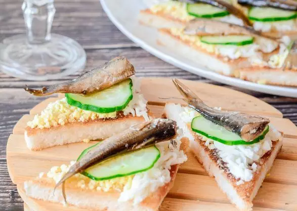 Triangular sandwiches with sprats, fresh cucumber and eggs on the table