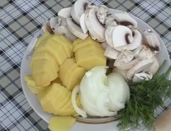 Prepared for cooking champignons, onions and potatoes on a plate with greens
