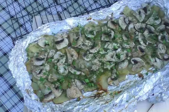 Potatoes cooked on a grill with mushrooms and onions on a sheet of aluminum foil