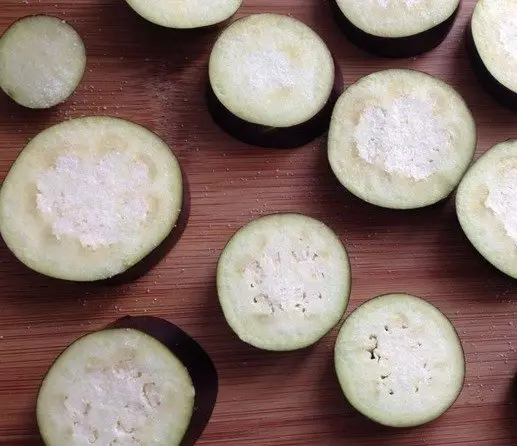 Circles of raw eggplant with salt on a wooden surface