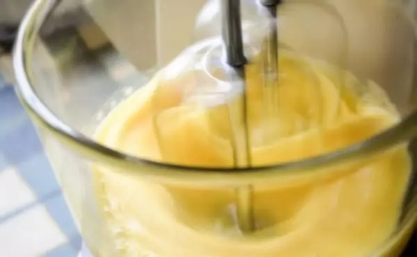 Piskade ägg med socker i transparent kapacitans och arbetskläder av mixer