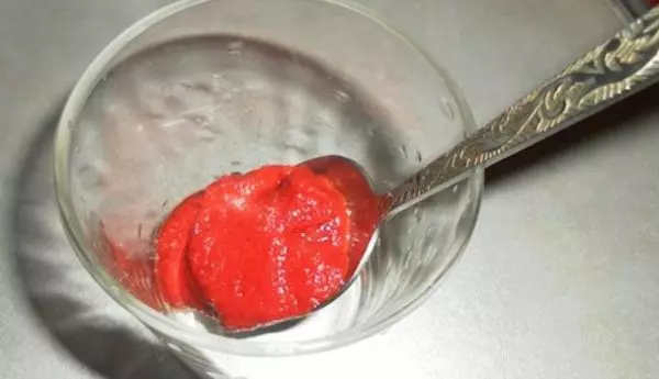 एक ग्लास कप मध्ये टोमॅटो पेस्ट सह चमच्याने