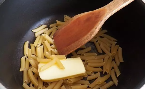 Pâtes sèches et un morceau de beurre dans une grande casserole avec spatule en bois