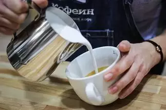 Eine breite Tasse wird von einem Eisenkugel Milch gegossen