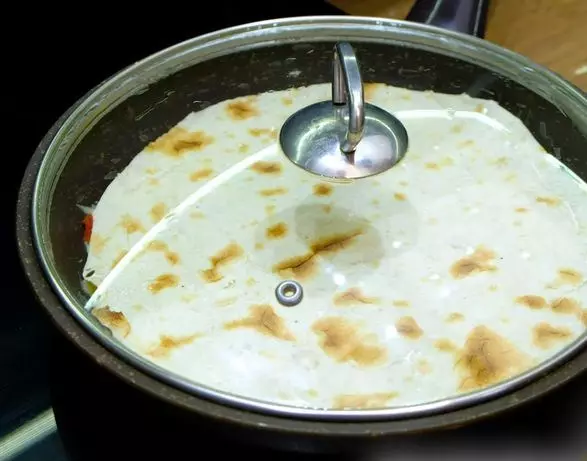 Billet from pita with filling in a frying pan with a glass lid