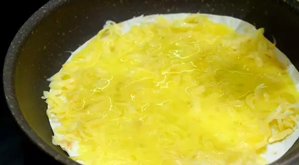 Casserole ronde de pita avec fromage râpé et oeufs cris dans une poêle à frire profonde