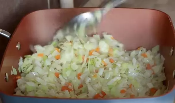 Grinding white cabbage with carrots and onions in a frying pan