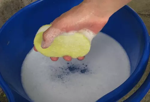 Gele spons nat in zeepoplossing in blauw bassin
