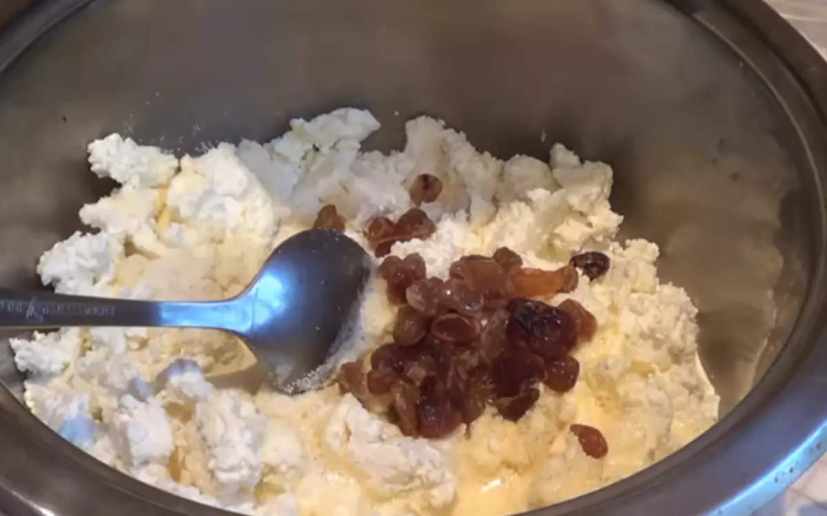 Cottage cheese, raisins and other ingredients of casserole in a metal bowl with a spoon