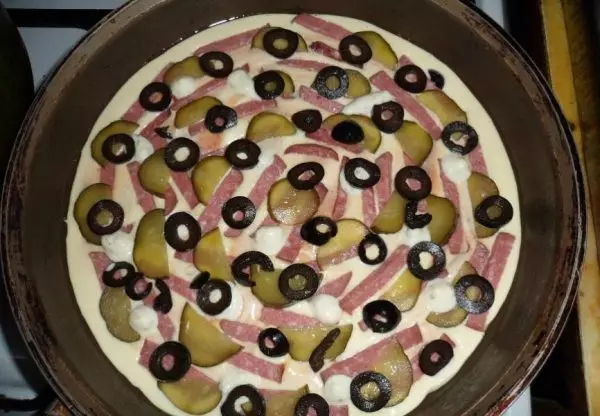Pizza dans une poêle à frire avec des olives, des concombre et des saucisses