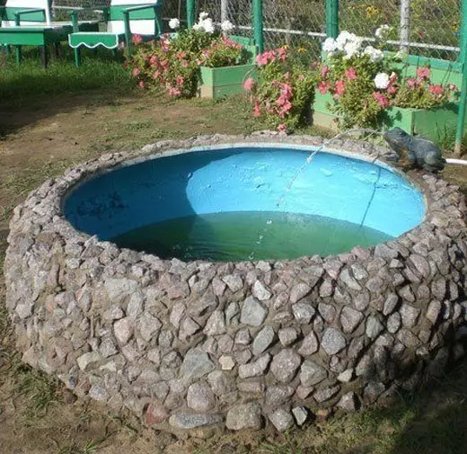 A piscina do velho pneu forrado com pedra