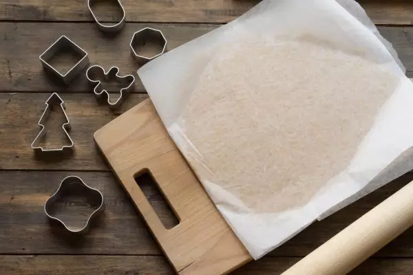 Camada de massa para ratos de gengibre entre folhas de papel de padaria e moldes de biscoitos metálicos