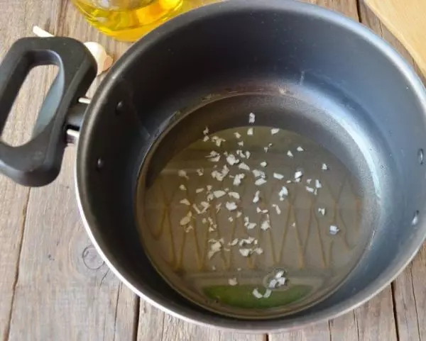 Bawang putih sing disigar ing panci kanthi minyak sayur ing meja kayu