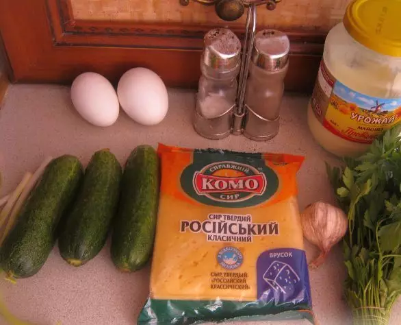 Produk kanggo masak salad saka endhog, keju, bawang ijo lan timun ing meja