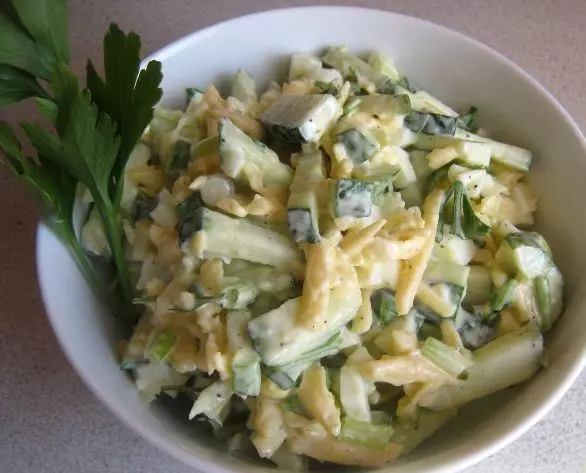Salāti no olām, zaļiem sīpoliem, svaigiem gurķiem un sieriem dziļā plāksnē uz galda