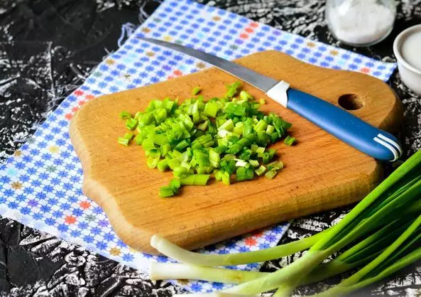 Cipolla verde tritata finemente su un tagliere di legno con un coltello