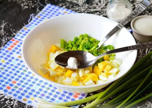 Lepel met zout in een diepe plaat met gekookte eieren en een groene boog