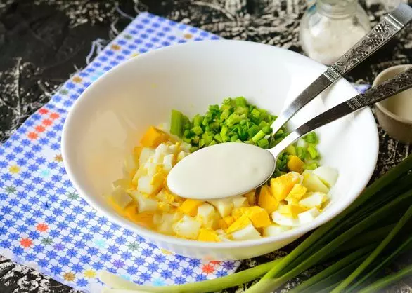 Spoon s kislo smetano v globoki plošči z mešanico jajc-čebule