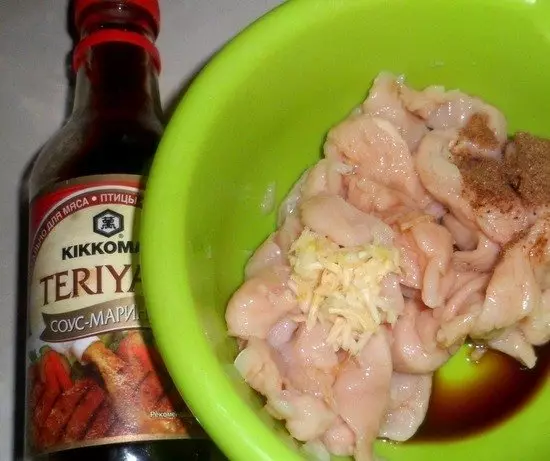 Sliced ​​raw chicken breasts with teriyaki sauce and garlic in a green plastic bowl