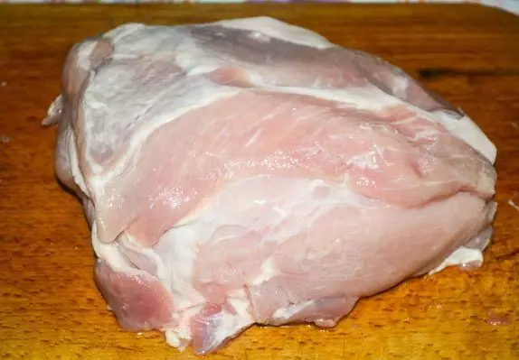 Një copë mish derri të papërpunuar në një sipërfaqe prej druri