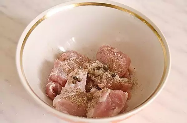 Feta të mishit të derrit të papërpunuar me erëza në një tas të thellë prej porcelani në tavolinë