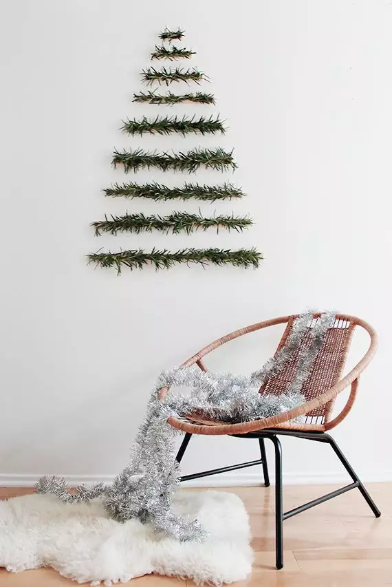 Σπιτικό χριστουγεννιάτικο δέντρο τριαντάφυλλο και φρέσκο ​​δεντρολίβανο στον τοίχο, ψάθινα καρέκλα και αφράτο λευκό χαλί