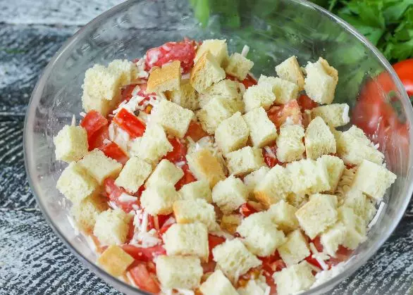 Salade met tamaties, gesmelte kaas en krakers in 'n glasbak op die tafel